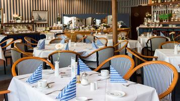 Um restaurante com cadeiras estofadas listradas, toalhas de mesa brancas e mesas de jantar bem arrumadas.