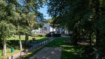 Uma trilha leva a um edifício com fachada de vidro, cercado por árvores e um gramado bem cuidado.