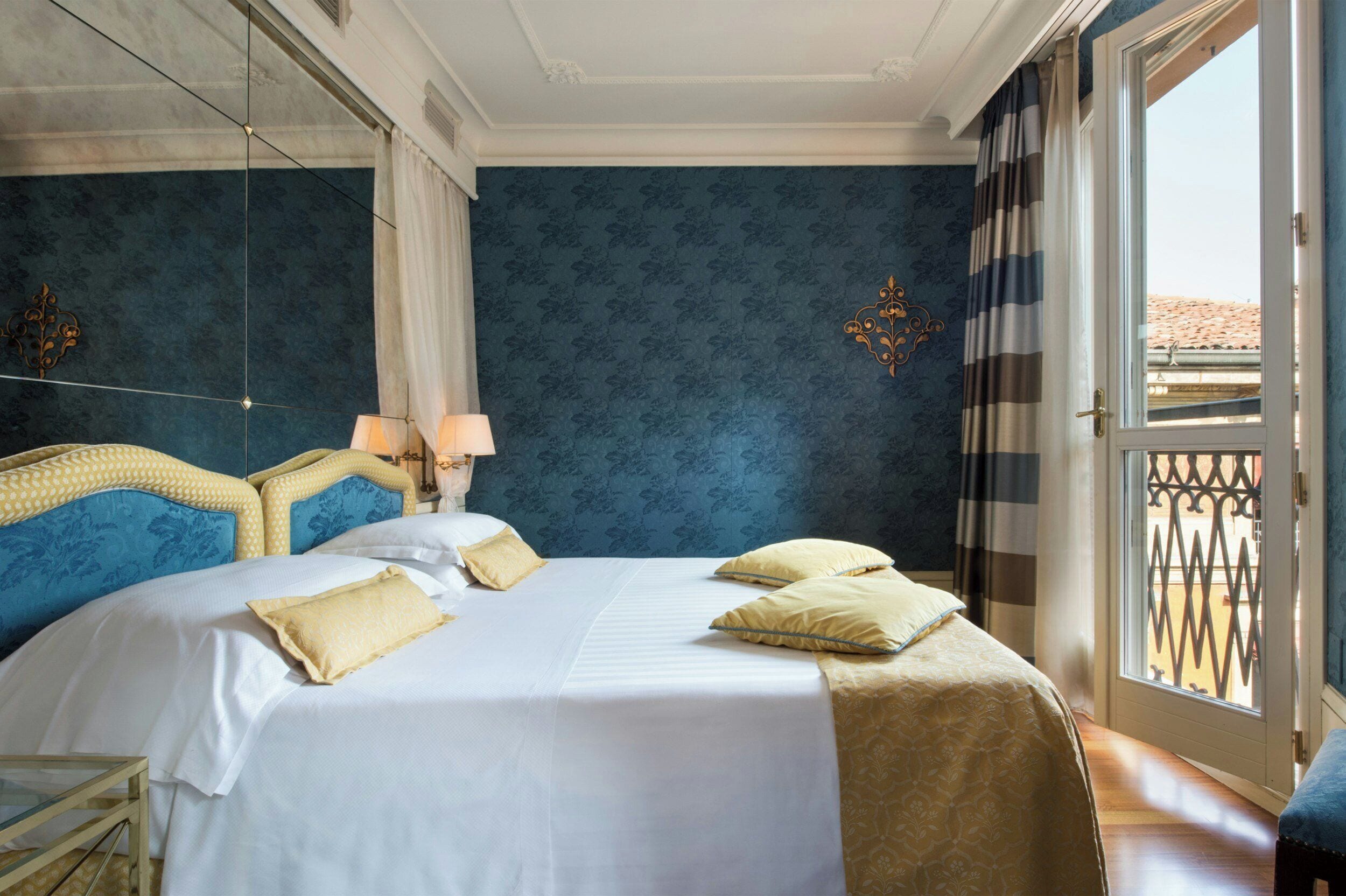 Quarto de hotel com uma cama grande, duas mesas de cabeceira, uma janela com cortinas e vista para o exterior.