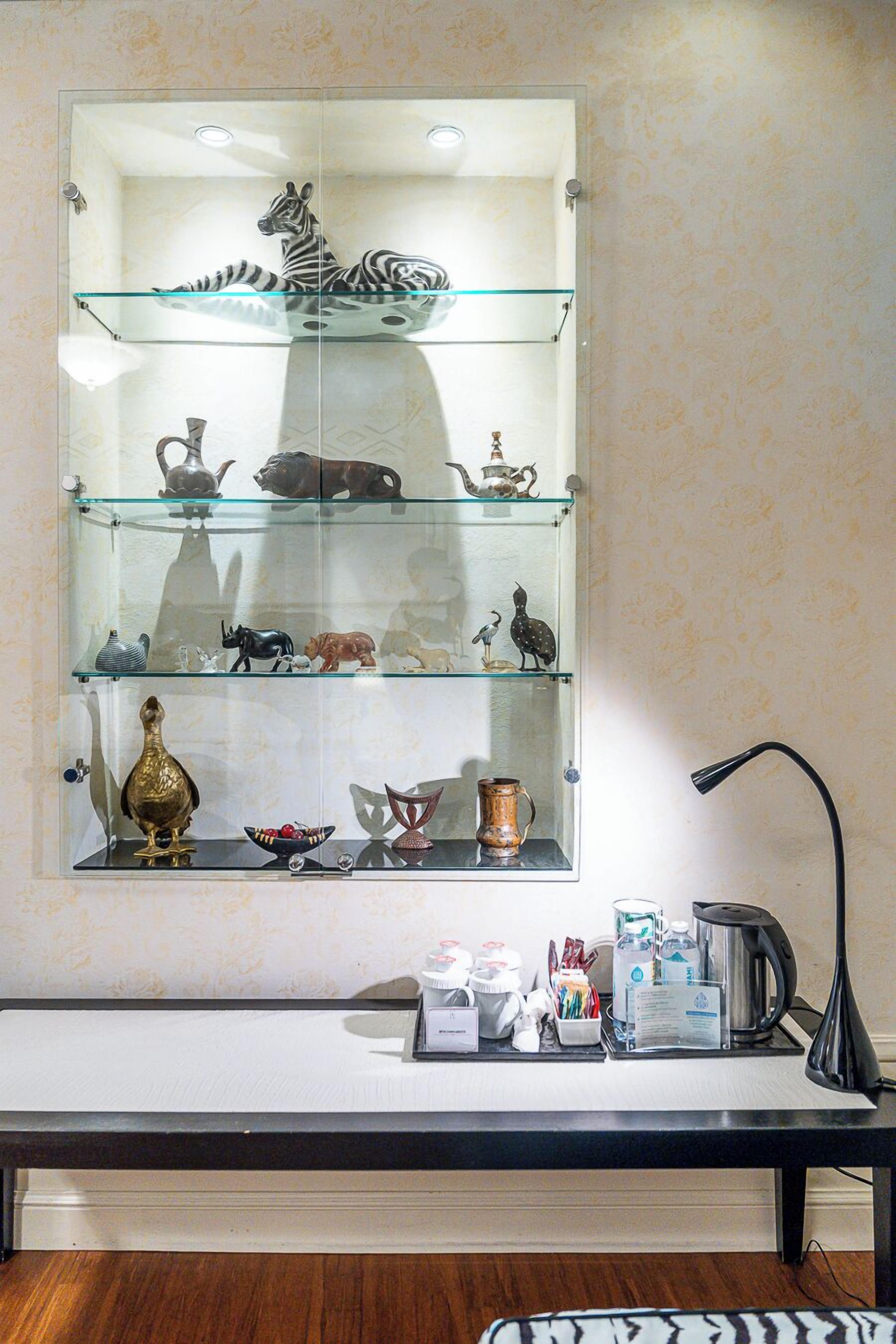 Casa de banho com um armário de vidro que exibe várias figuras de animais e uma área de lavatório com produtos de higiene e uma chaleira.