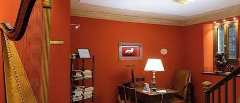 Um quarto com uma harpa, uma escrivaninha com uma luminária, uma cadeira e uma estante de livros.