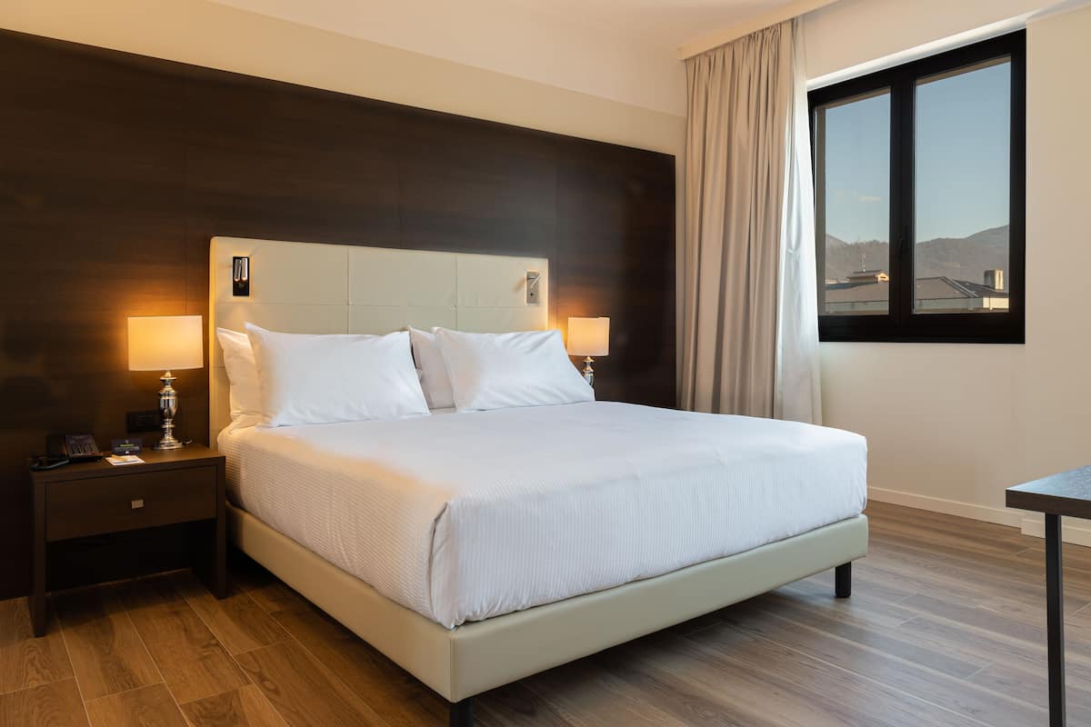Uma cama bem arrumada com lençóis brancos, uma cabeceira de madeira escura e uma mesa de cabeceira com abajur.