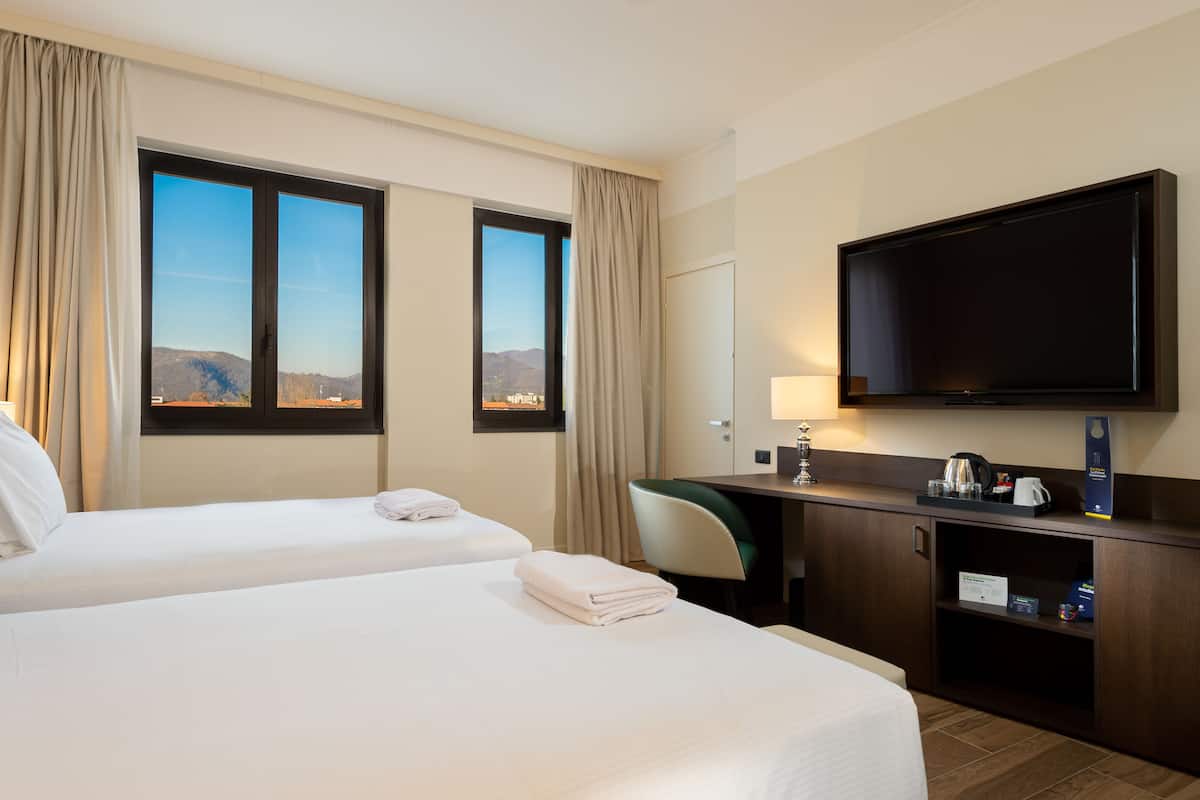 Quarto de hotel com duas camas, uma escrivaninha, televisão e vista para as montanhas.