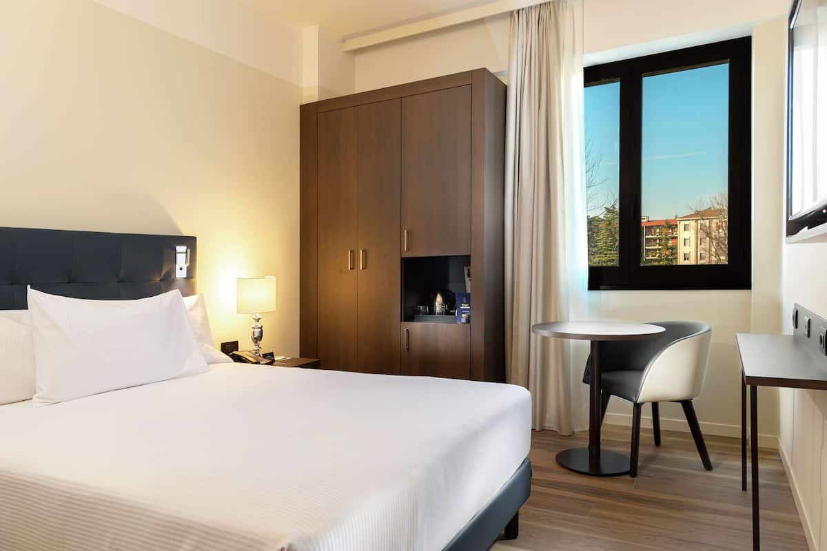 Quarto de hotel com uma cama grande, uma mesa, uma cadeira e um guarda-roupa.