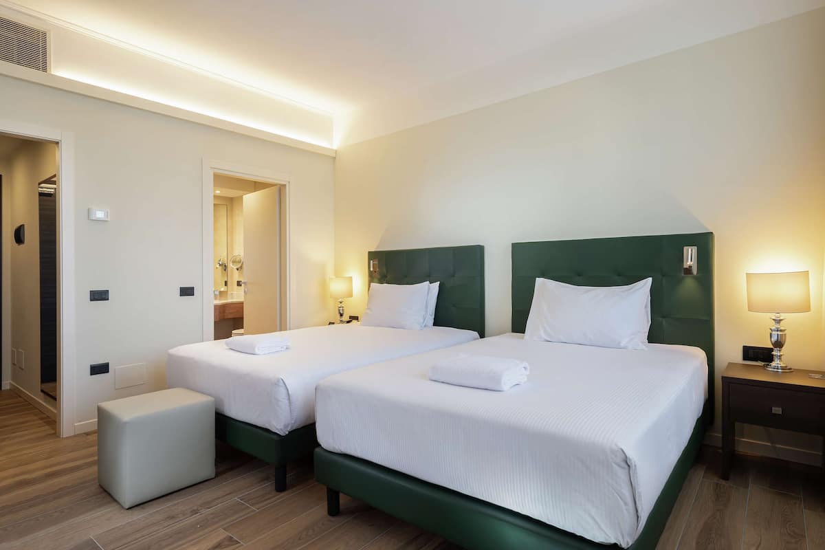 Quarto de hotel com duas camas, um espaço de estar pequeno e um banheiro visível por uma porta aberta.
