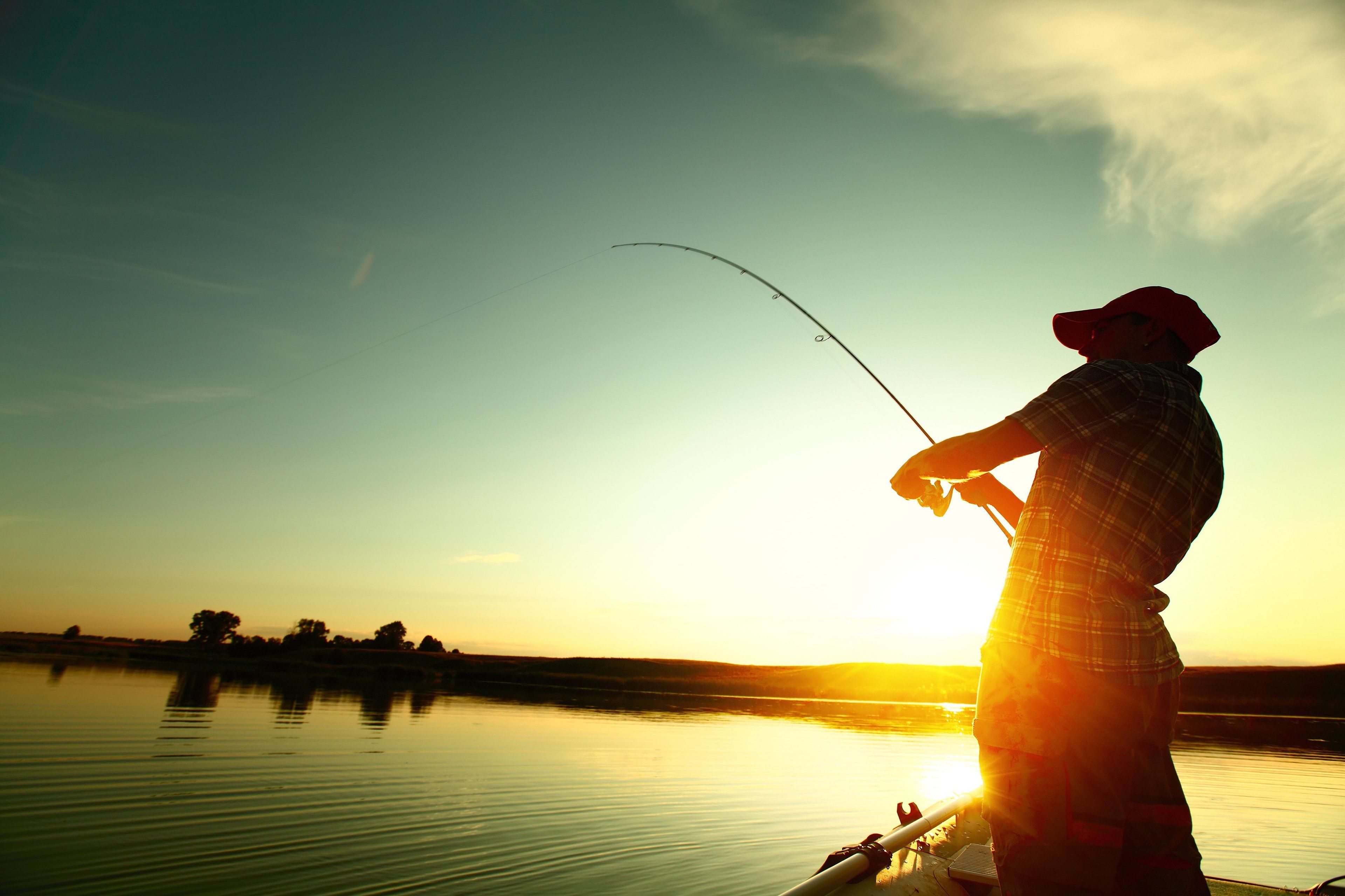 Pessoa pescando ao pôr do sol, com água calma e céu limpo.