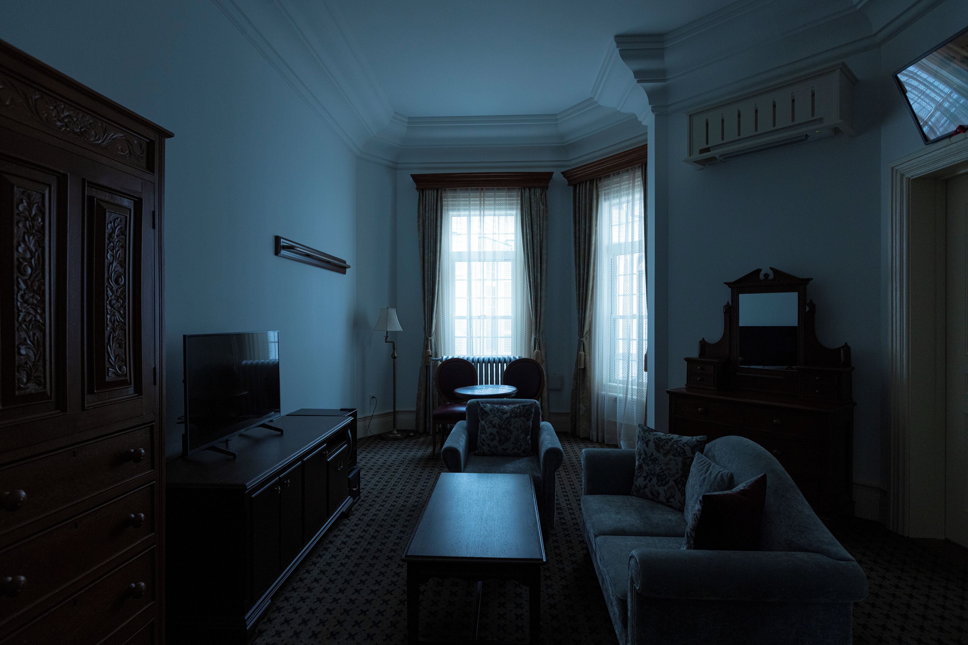 Um quarto com iluminação fraca, com televisão, sofá, mesa de centro e armário.
