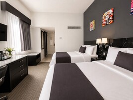 Quarto de hotel com duas camas, uma escrivaninha, toucador e obras de arte nas paredes.