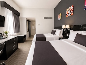 Quarto de hotel com duas camas, uma escrivaninha, toucador e obras de arte nas paredes.