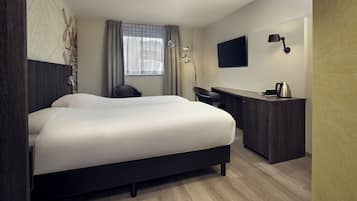 Quarto de hotel moderno com uma cama grande, uma escrivaninha, uma cadeira, uma televisão e uma cafeteira.