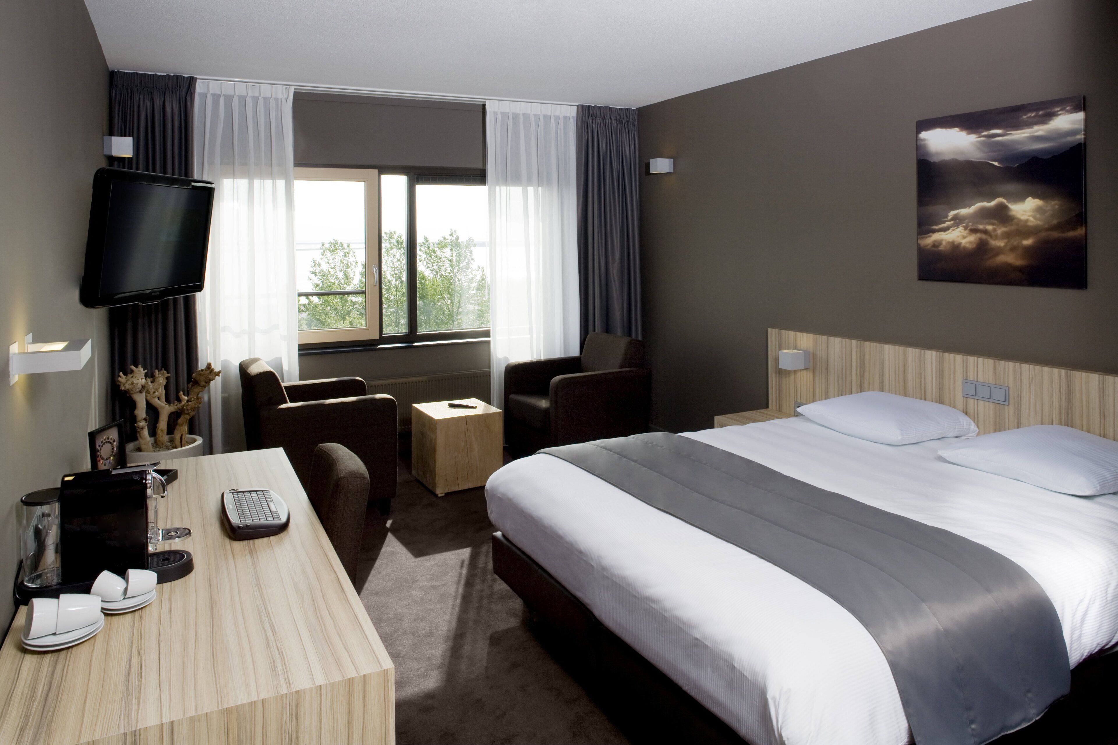Quarto de hotel com uma cama grande, uma escrivaninha com computador, televisão e janela com cortinas.