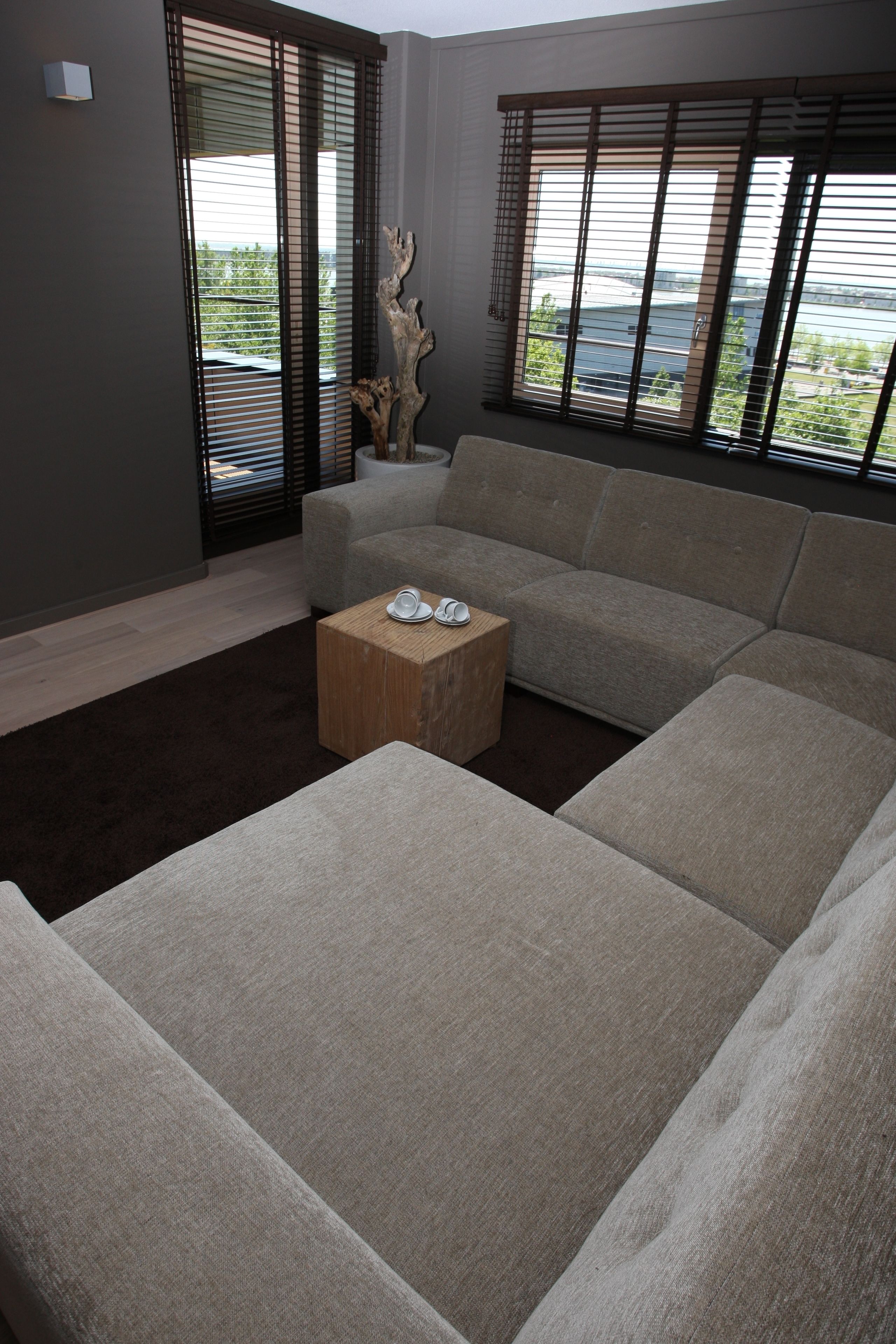 Uma sala de estar moderna com sofá seccional, mesa de centro de madeira e uma escultura de árvore decorativa.
