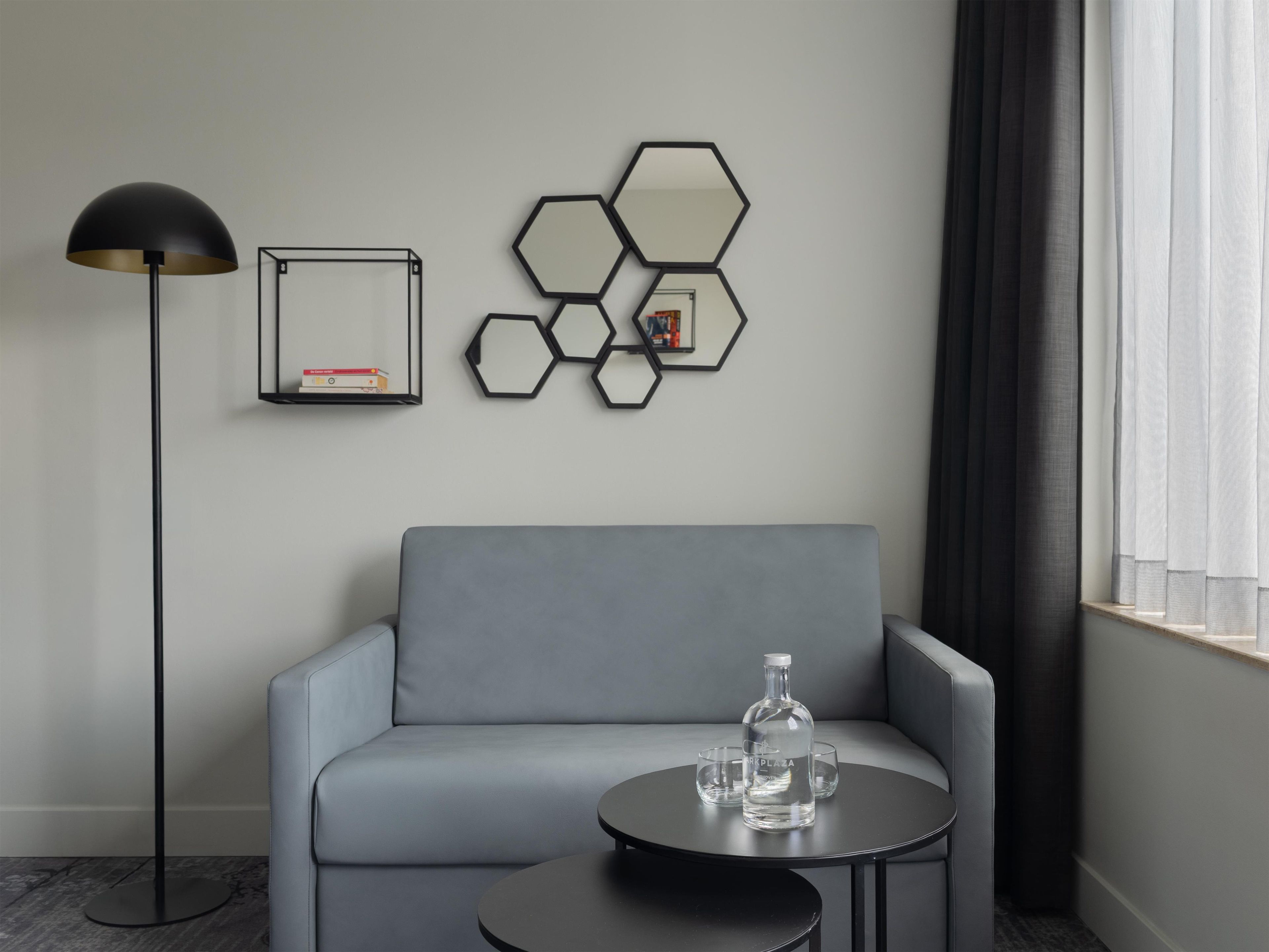 Sala de estar moderna com um sofá cinzento, uma mesa de centro redonda, um abajur e arte de parede hexagonal.
