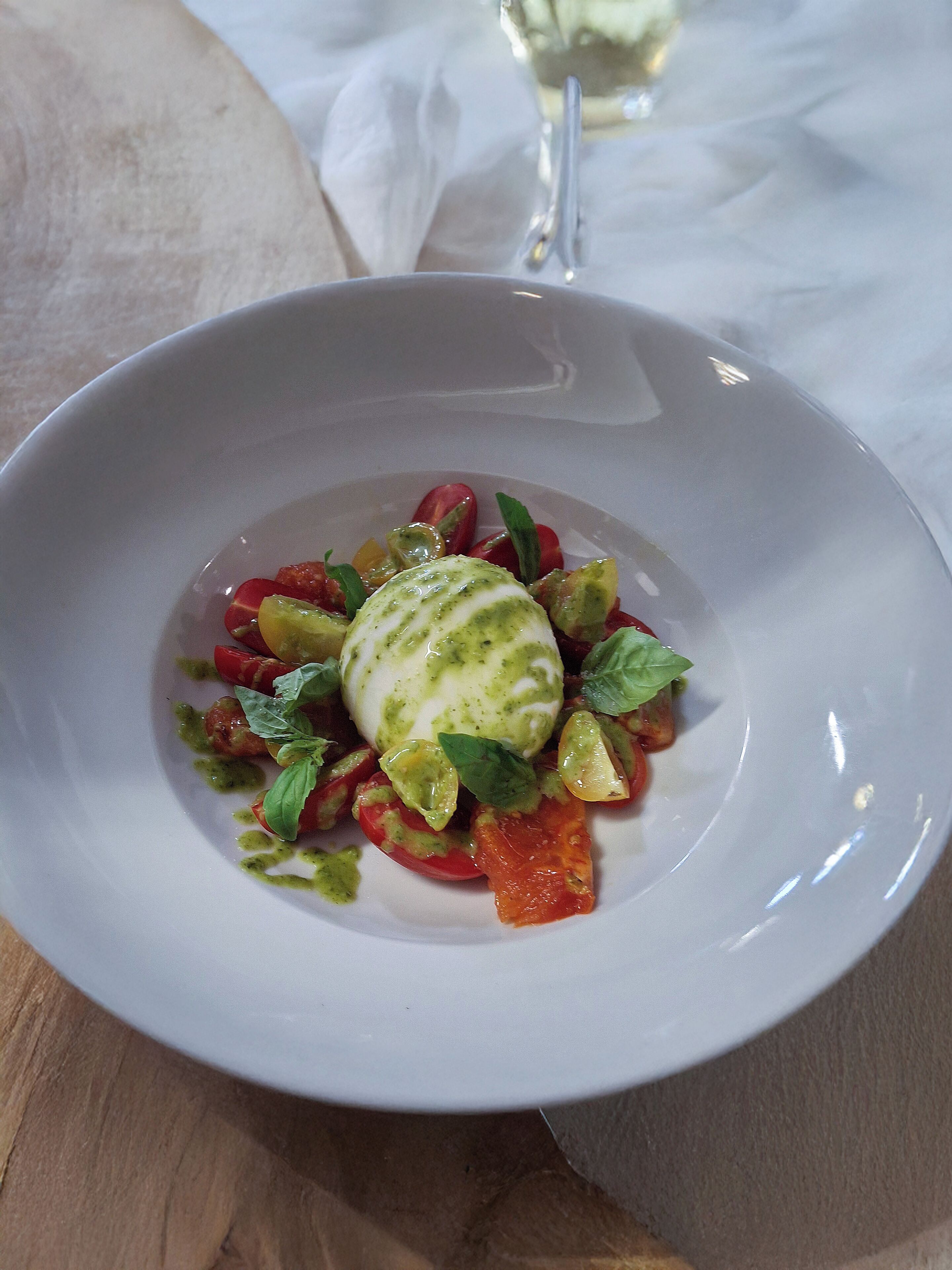 Prato branco com sobremesa de uma bola de sorvete, tomates frescos e folhas de manjericão.