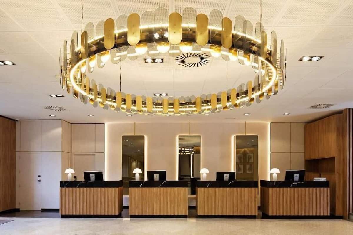 Uma área de recepção de hotel com um lustre circular, balcões de recepção e uma parede espelhada.