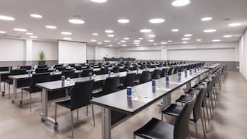 Uma sala de conferências com fileiras de mesas e cadeiras, equipada com garrafas de água e placas de identificação.