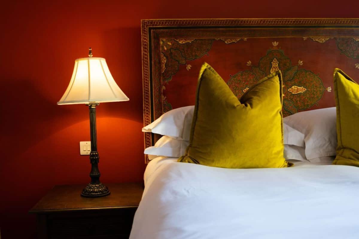 Quarto de hotel com uma cama, uma mesa de cabeceira com abajur e uma cabeceira decorativa.