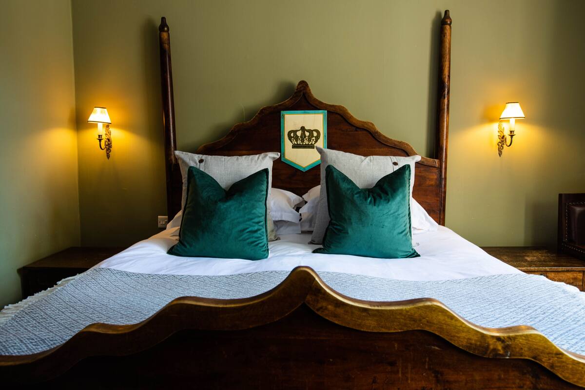 Uma cama com dossel e cabeceira de madeira, duas luminárias fixadas na parede e um emblema decorativo na cabeceira.