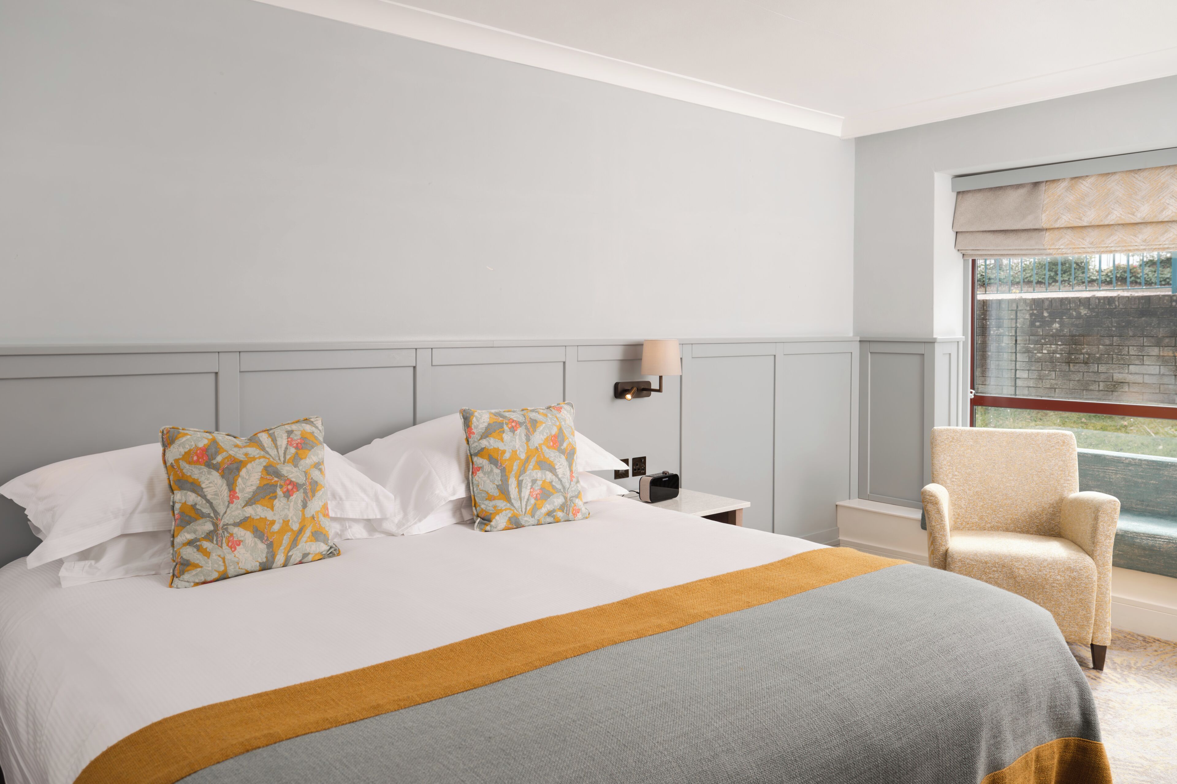 Quarto de hotel com cama, duas almofadas, mesa de cabeceira, luminária, cadeira e janela com vista.