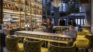 Um bar com um bartender preparando uma bebida, prateleiras de bebidas alcoólicas e cadeiras amarelas.