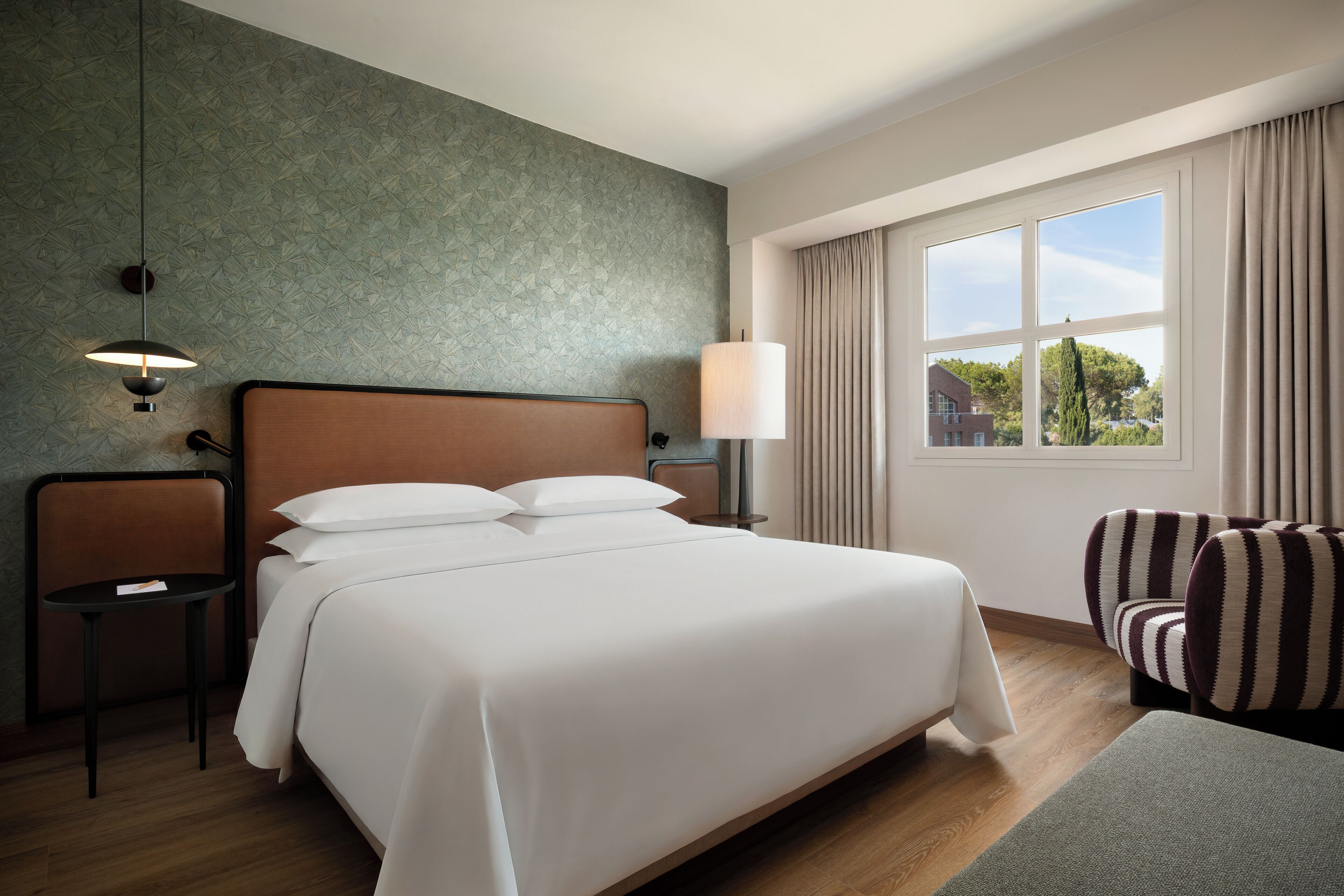 Quarto de hotel com uma cama, uma cadeira, um abajur, uma janela e vista para o exterior.