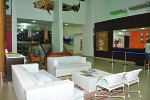 Um lobby amplo com sofás e cadeiras brancas, um balcão de recepção e obras de arte nas paredes.