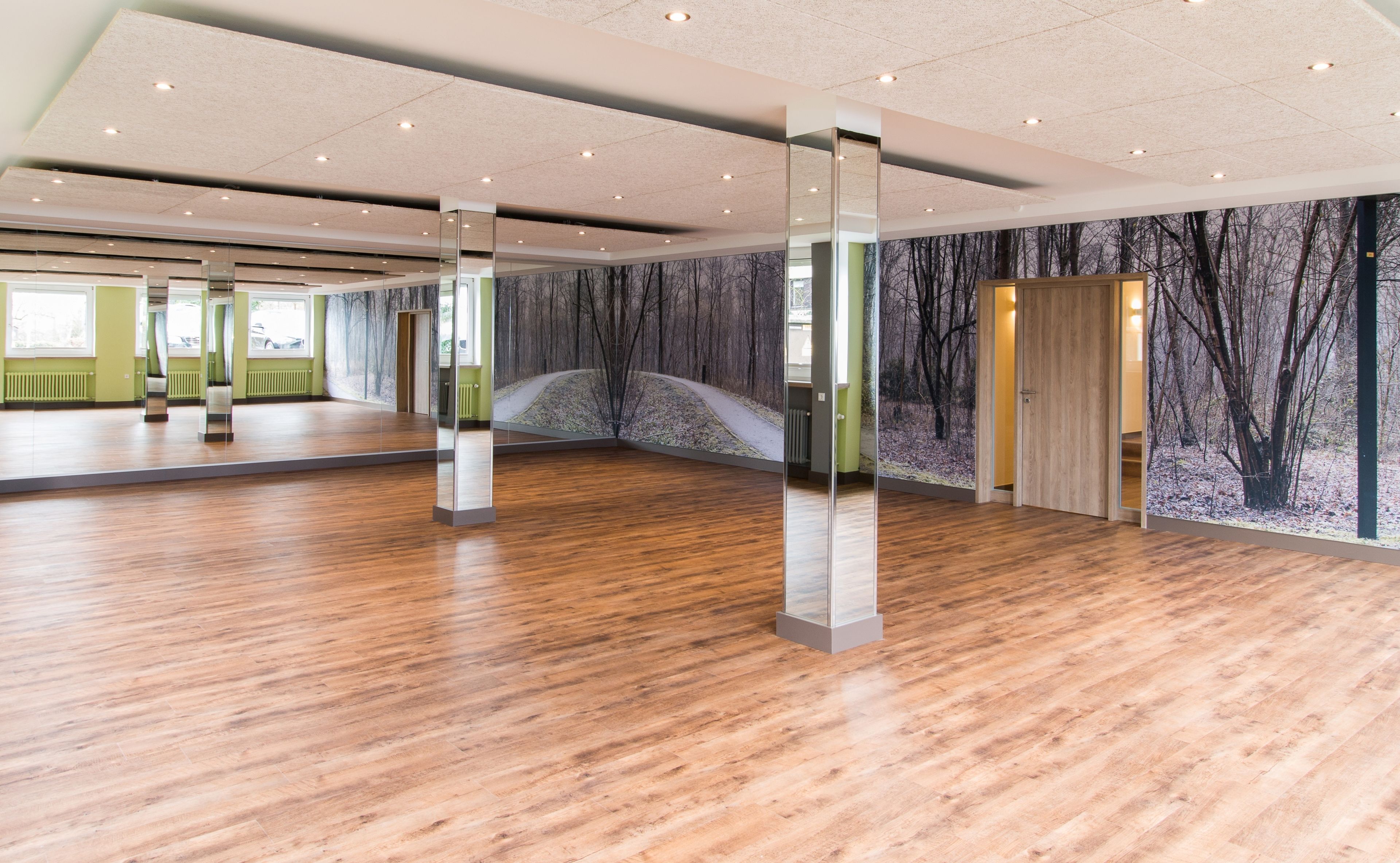 Quarto espaçoso com piso de madeira, grandes espelhos e um mural de árvores na parede.