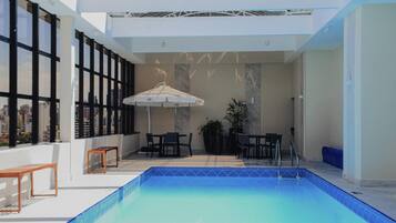 Piscina no terraço com vista para o horizonte da cidade, área de estar externa e um espaço coberto com varanda.