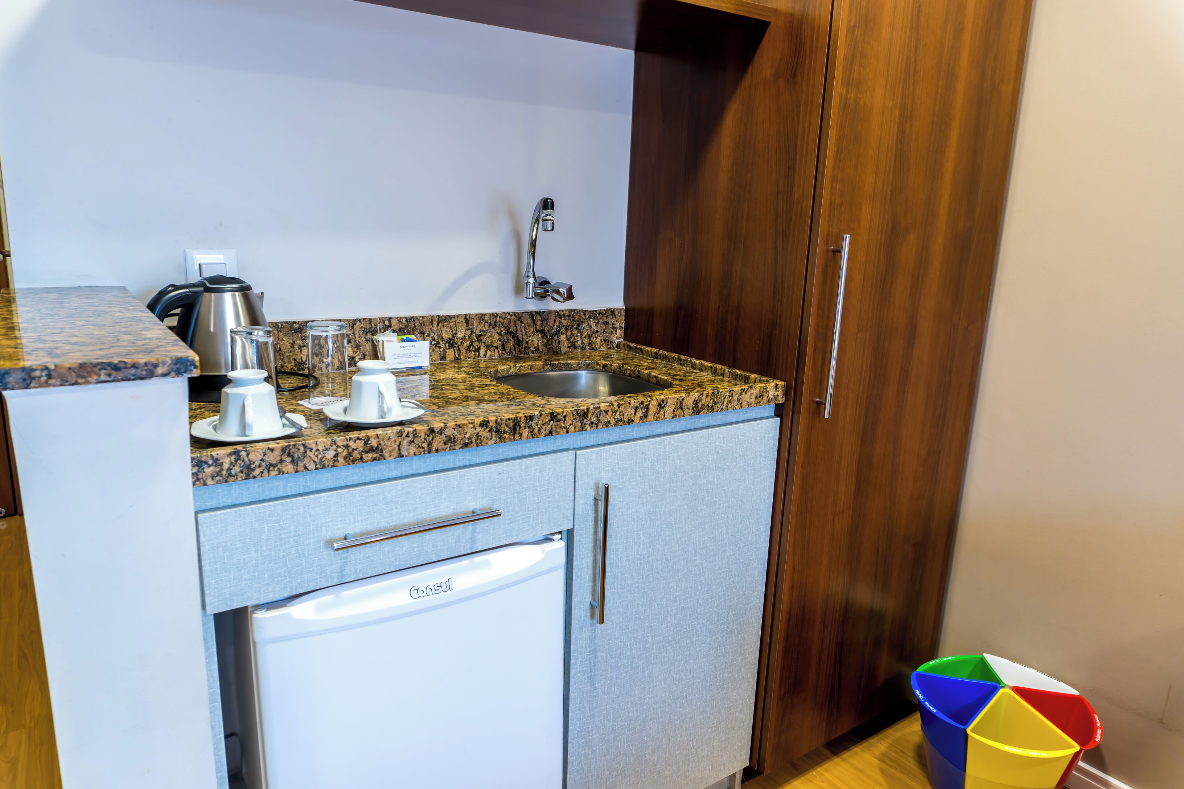Uma cozinha compacta equipada com uma pia de aço inoxidável, uma cafeteira e um pequeno frigorífico.