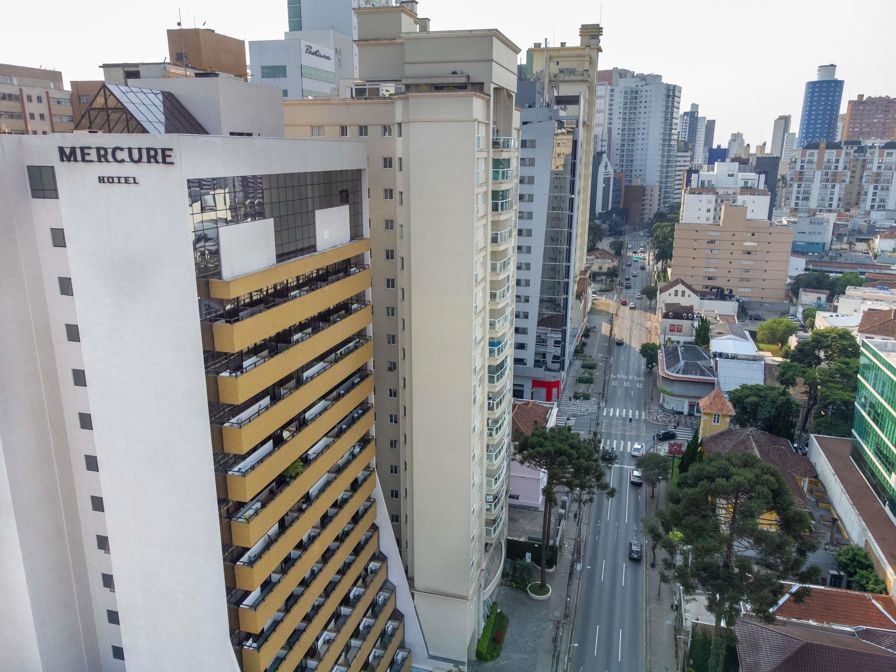 Um hotel de grande porte com vários andares, um letreiro chamativo 'Mercure' e um horizonte urbano ao fundo.