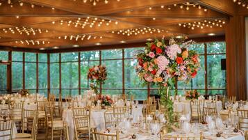 Uma sala de banquetes com mesas redondas, cadeiras douradas e centros de mesa florais.