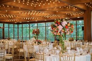 Uma sala de banquetes com mesas redondas, cadeiras douradas e centros de mesa florais.
