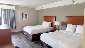 Quarto de hotel com duas camas, uma escrivaninha, uma cadeira e um quadro na parede.