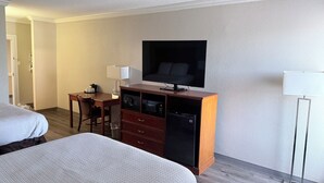 Quarto de hotel com cama, escrivaninha com luminária, televisão e minibar.