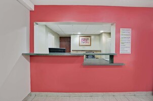 Uma área de recepção com parede vermelha, balcão de recepção e um quadro na parede.