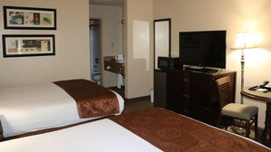 Quarto de hotel com duas camas, uma secretária com cadeira, televisão e candeeiro.