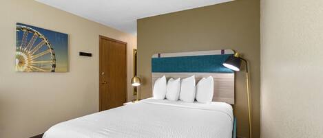 Quarto de hotel com uma cama, cabeceira, luminária fixada na parede, porta e pintura na parede.