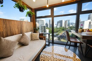 Uma sala de estar moderna com um sofá, uma mesa de jantar e vista para o horizonte urbano através de amplas janelas.