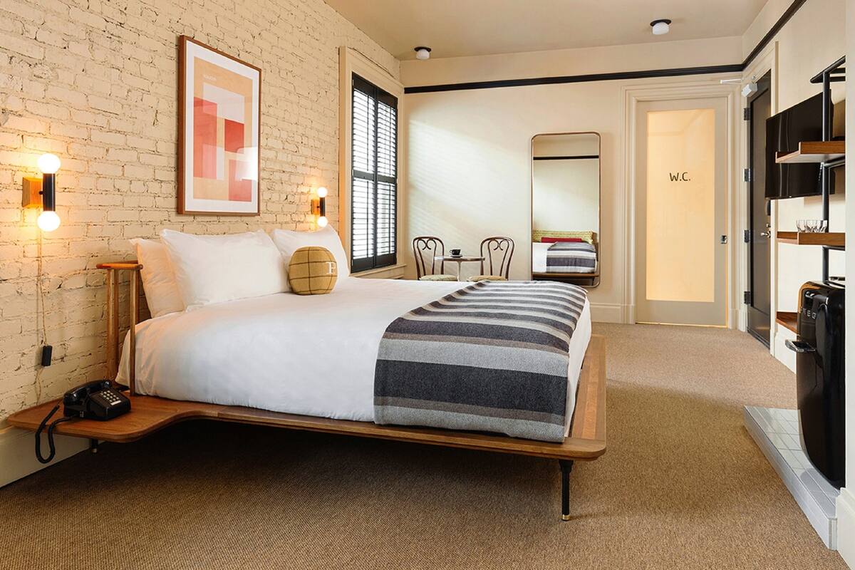 Quarto moderno com cama, mesa de cabeceira, abajur e parede de tijolos.