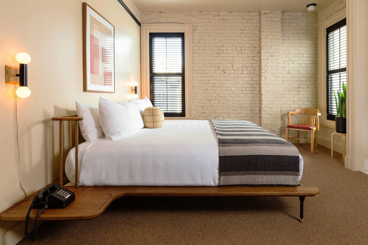 Quarto moderno com uma cama grande, telefone na mesa de cabeceira, quadro na parede e parede de tijolos.