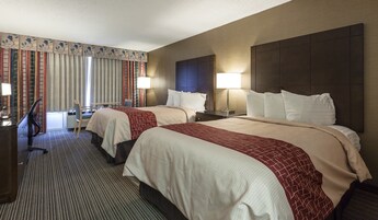 Quarto de hotel com duas camas, uma escrivaninha e uma cadeira.