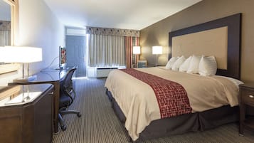 Quarto de hotel com cama, escrivaninha, cadeira e televisão.