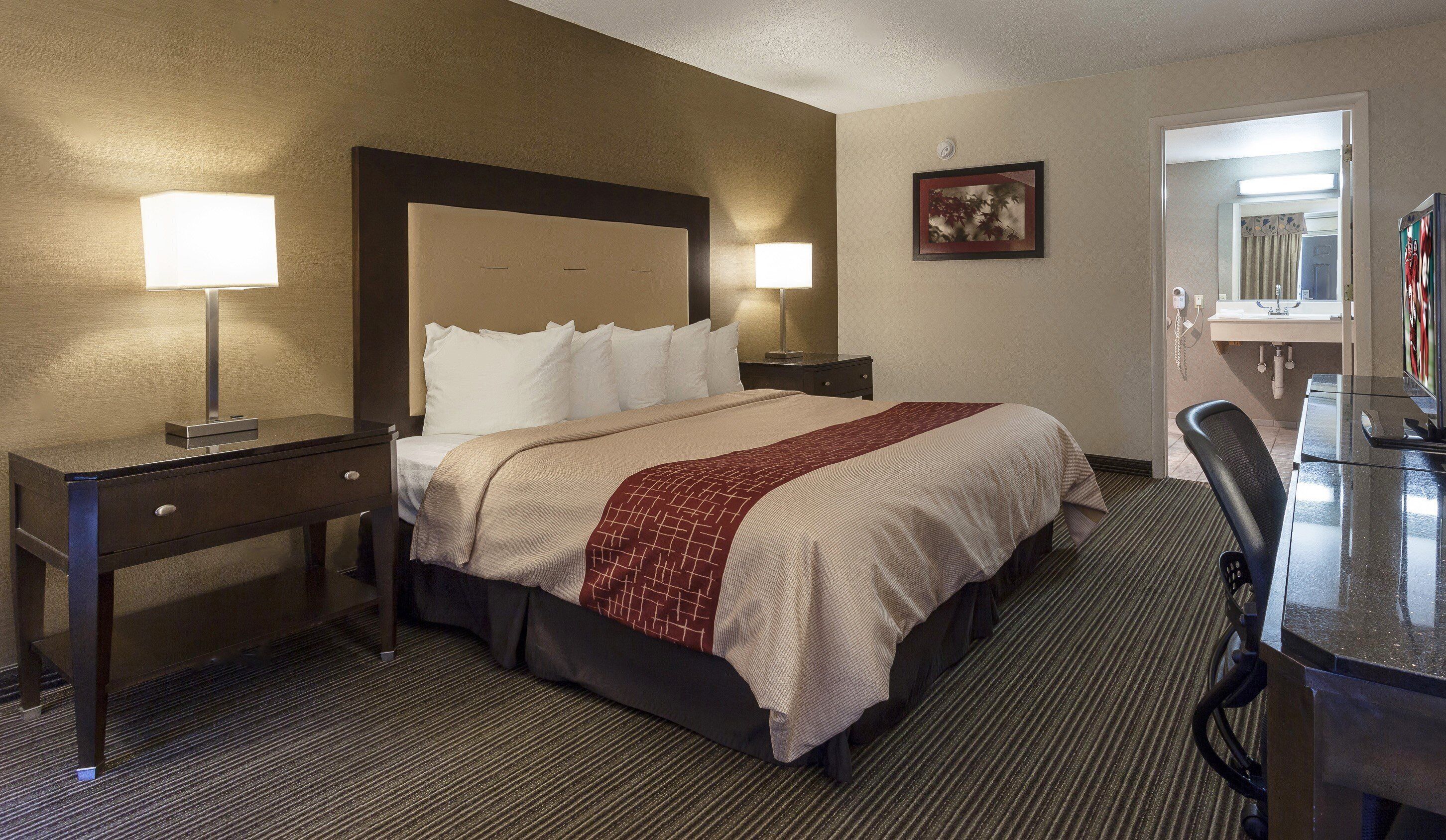 Quarto de hotel com cama, mesas de cabeceira, luminárias, escrivaninha e uma cadeira.