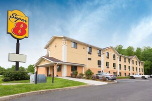 Um hotel Super 8 com um edifício de dois andares, estacionamento e área gramada com arbustos.
