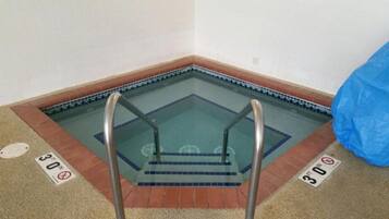 Pequena piscina interior com fundo de vidro, duas escadas de metal e uma lona azul à direita.