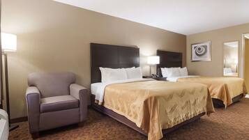 Quarto de hotel com duas camas, uma cadeira e um abajur.