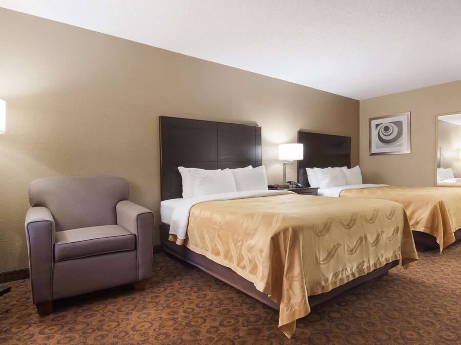 Quarto de hotel com duas camas, uma cadeira e um abajur.