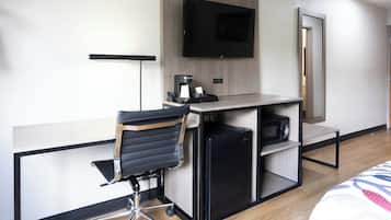 Quarto de hotel com uma escrivaninha, uma cadeira, televisão na parede, máquina de café e micro-ondas.