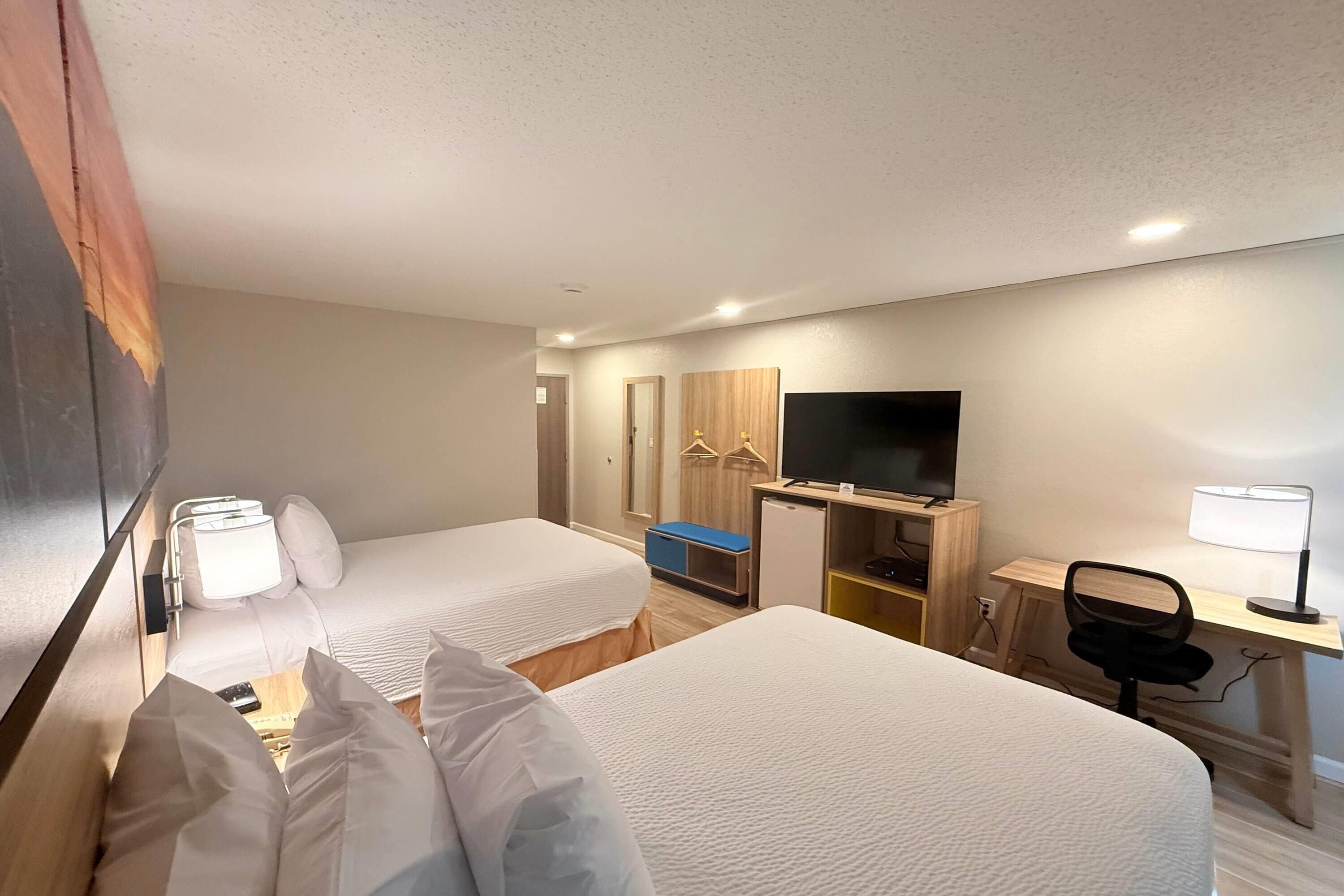 Quarto de hotel com duas camas, uma escrivaninha com computador, televisão e guarda-roupa.