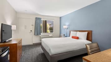 Quarto de hotel com cama, escrivaninha, televisão e janela com cortinas.